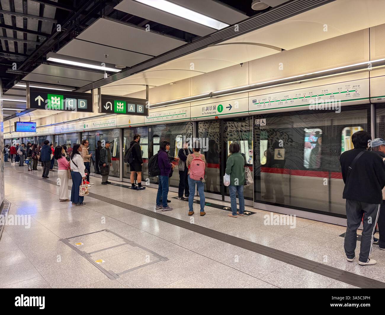 Commuters await a train at a platform in a Hong Kong MTR station ...