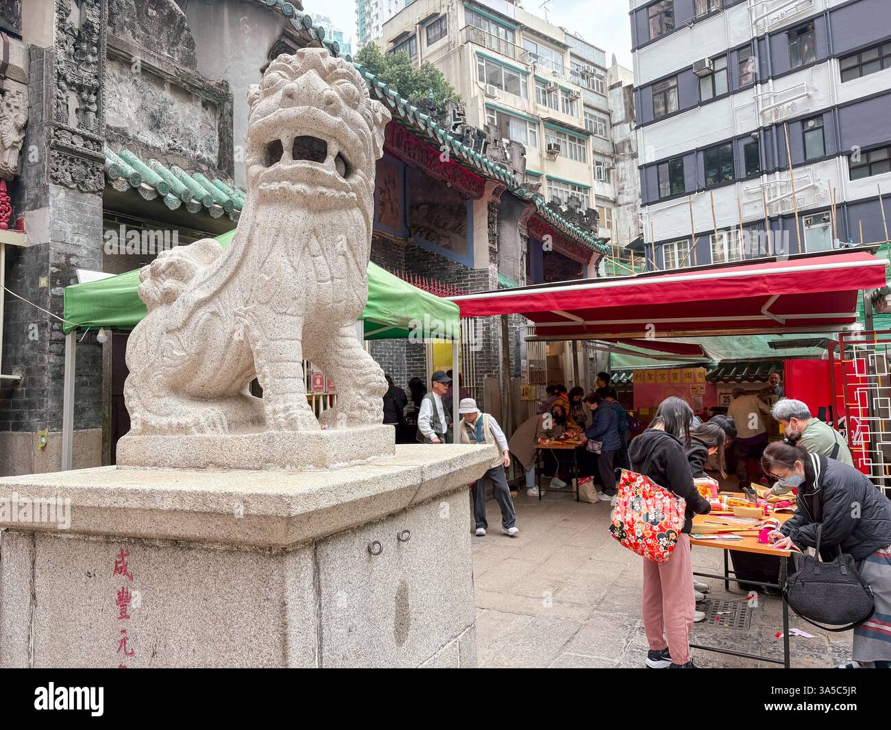 Stone lion statue at Man Mo Temple in Hong Kong. People praying and ...