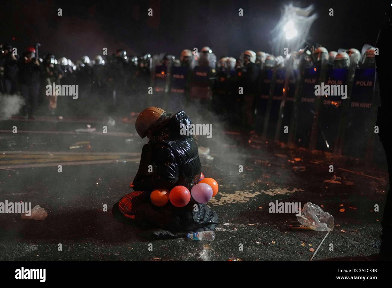 A protester sits on her knees as riot police stand guard during a ...