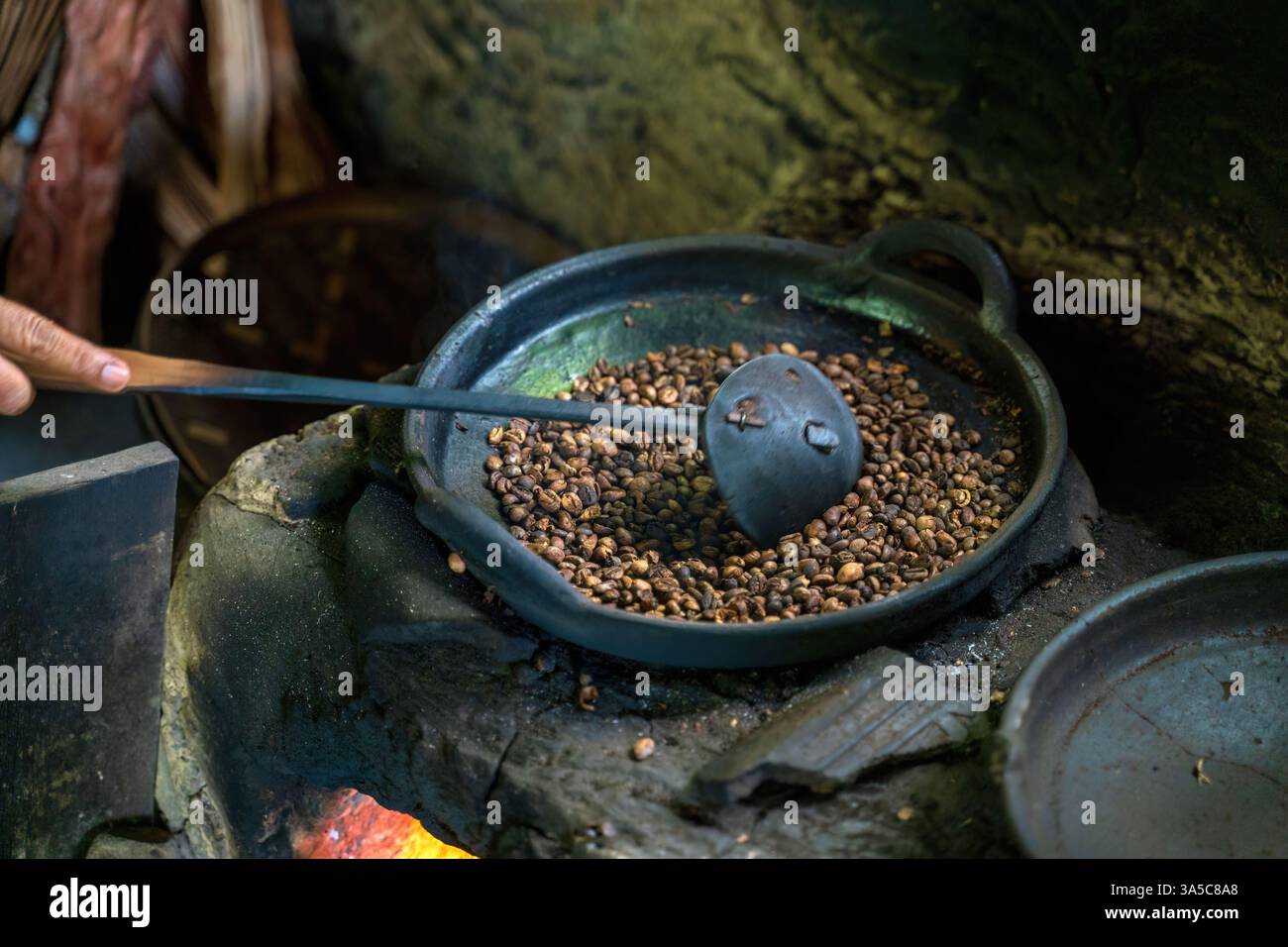 Hand stirring roasting coffee beans in a dark, rustic pan over a wood ...