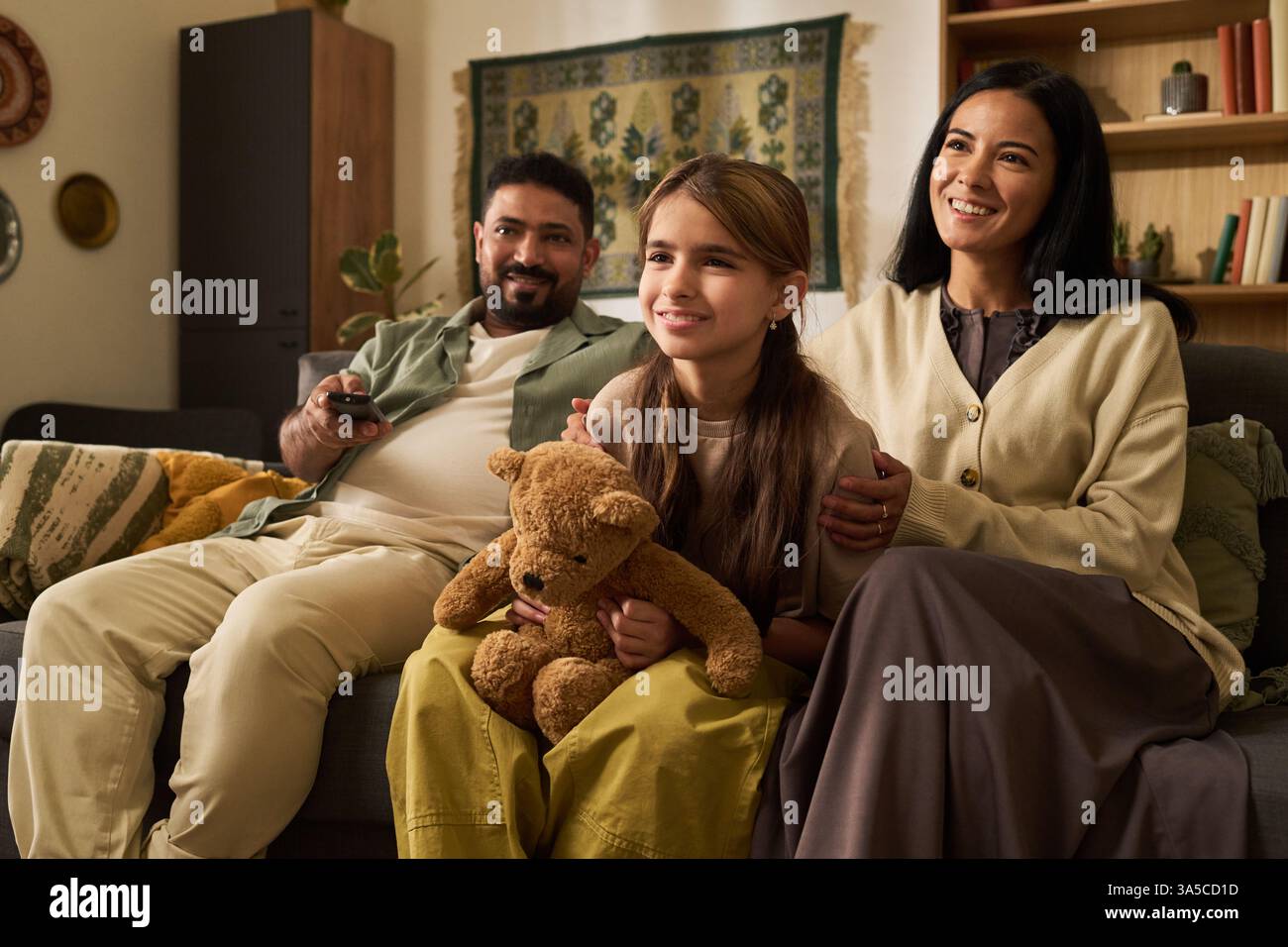 Family sitting on a cozy couch, smiling and watching TV together in ...