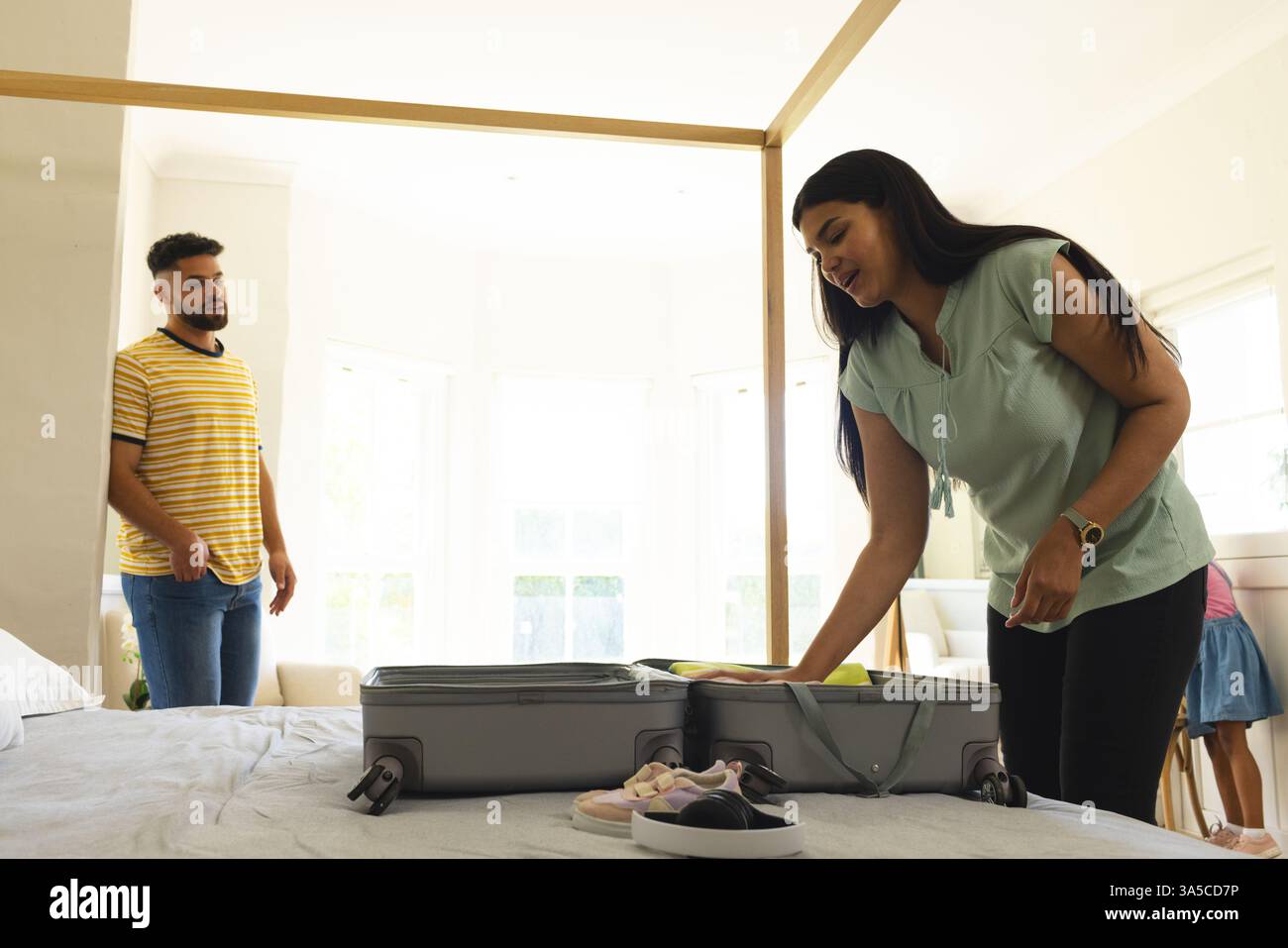 Woman packing suitcase on bed while man watching in bright bedroom ...