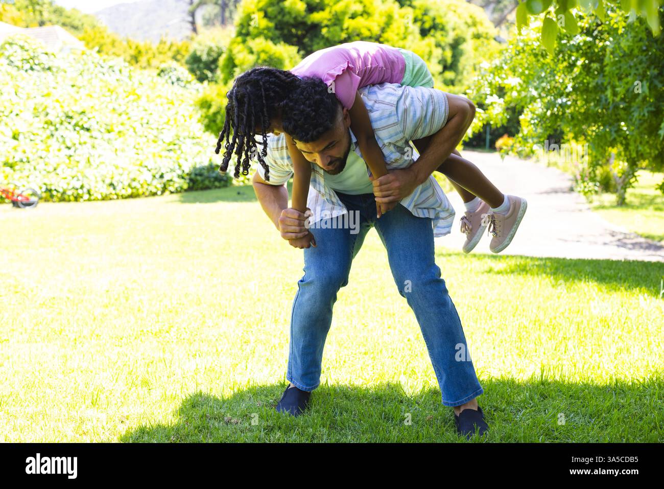 Father giving daughter piggyback ride in sunny park, both laughing ...
