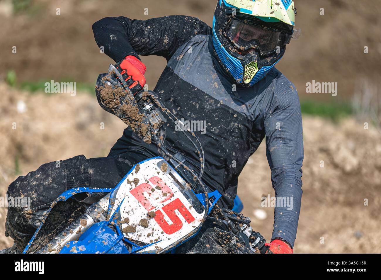 Motocross rider is covered in mud as he races his dirt bike through a ...