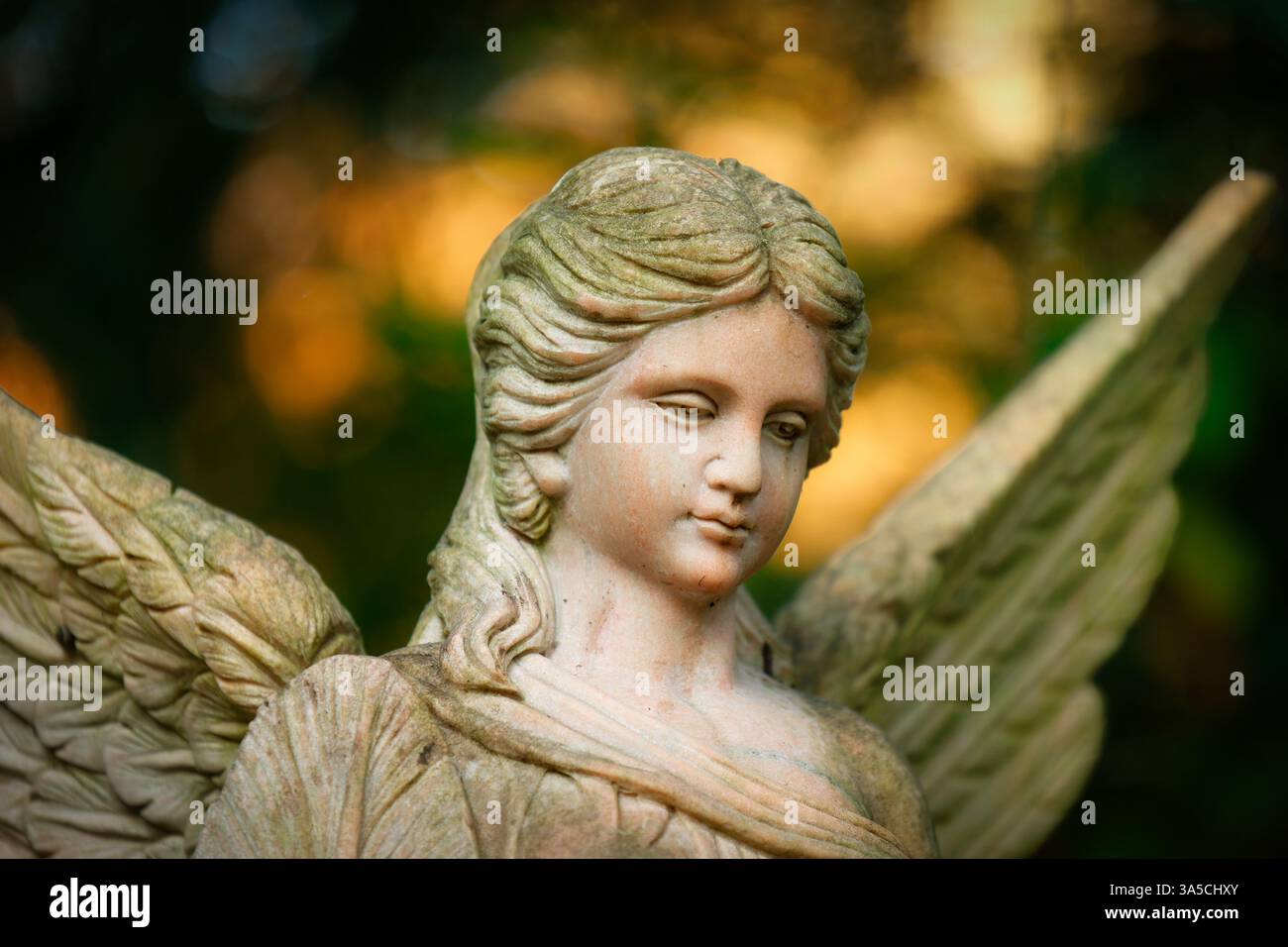Angel statue with wings against a blurred background of green and gold ...