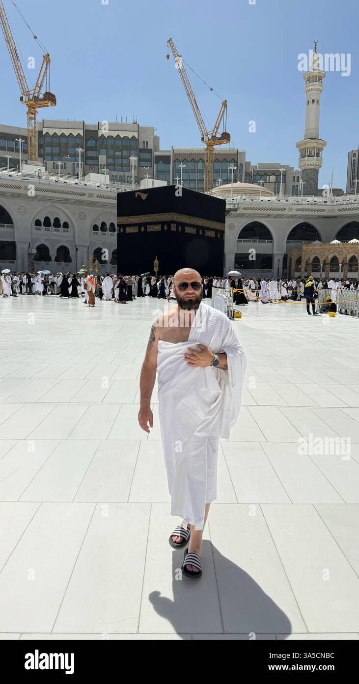 A bald man poses for a photo in front of the Kaaba at noon after ...