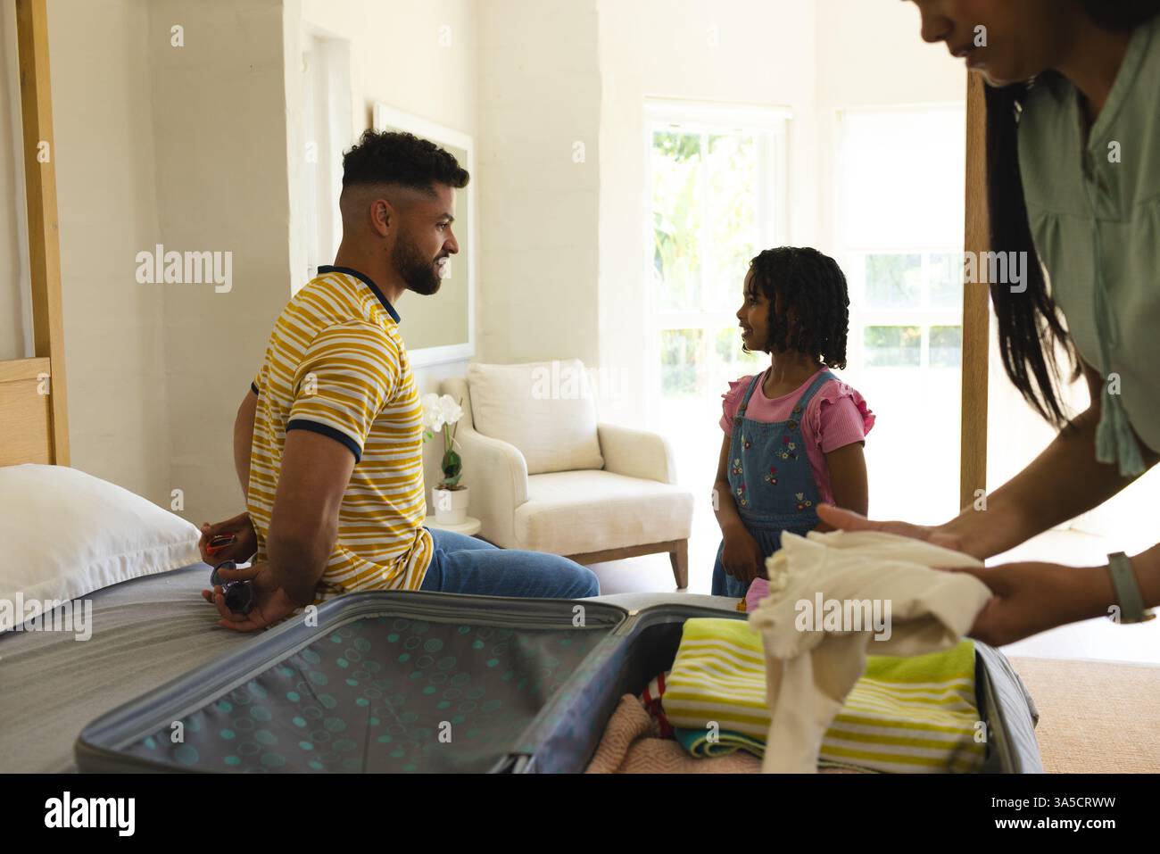 Father and daughter talking while mother packs suitcase at home, preparing for trip Stock Photo ...