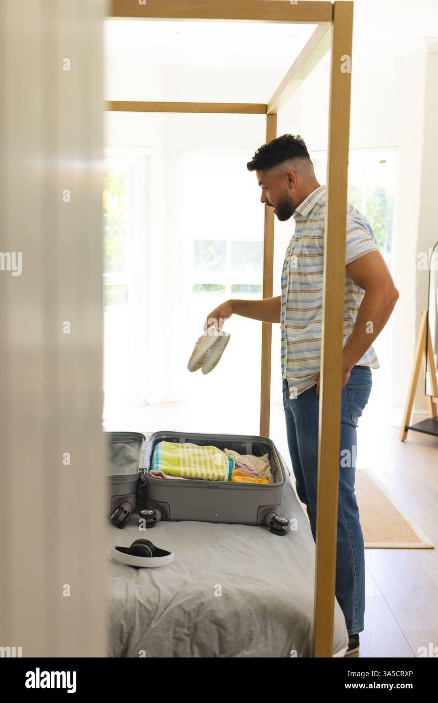 Man packing suitcase with clothes and shoes in bright bedroom ...