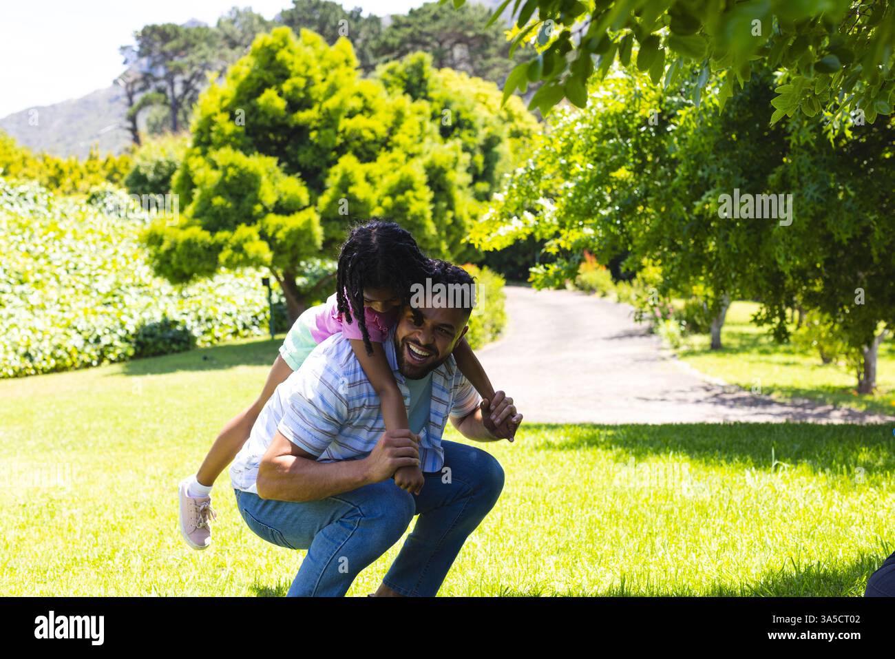 In sunny park, father giving daughter piggyback ride, both laughing ...