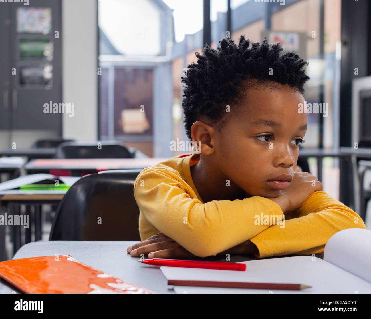 In school, thoughtful child resting head on desk, surrounded by books ...