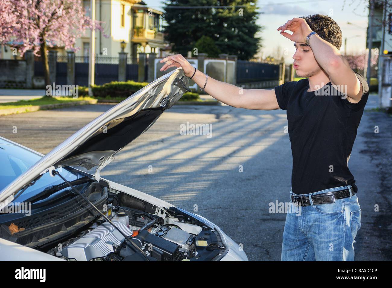 Handsome young man trying to repair a car engine, looking inside open ...