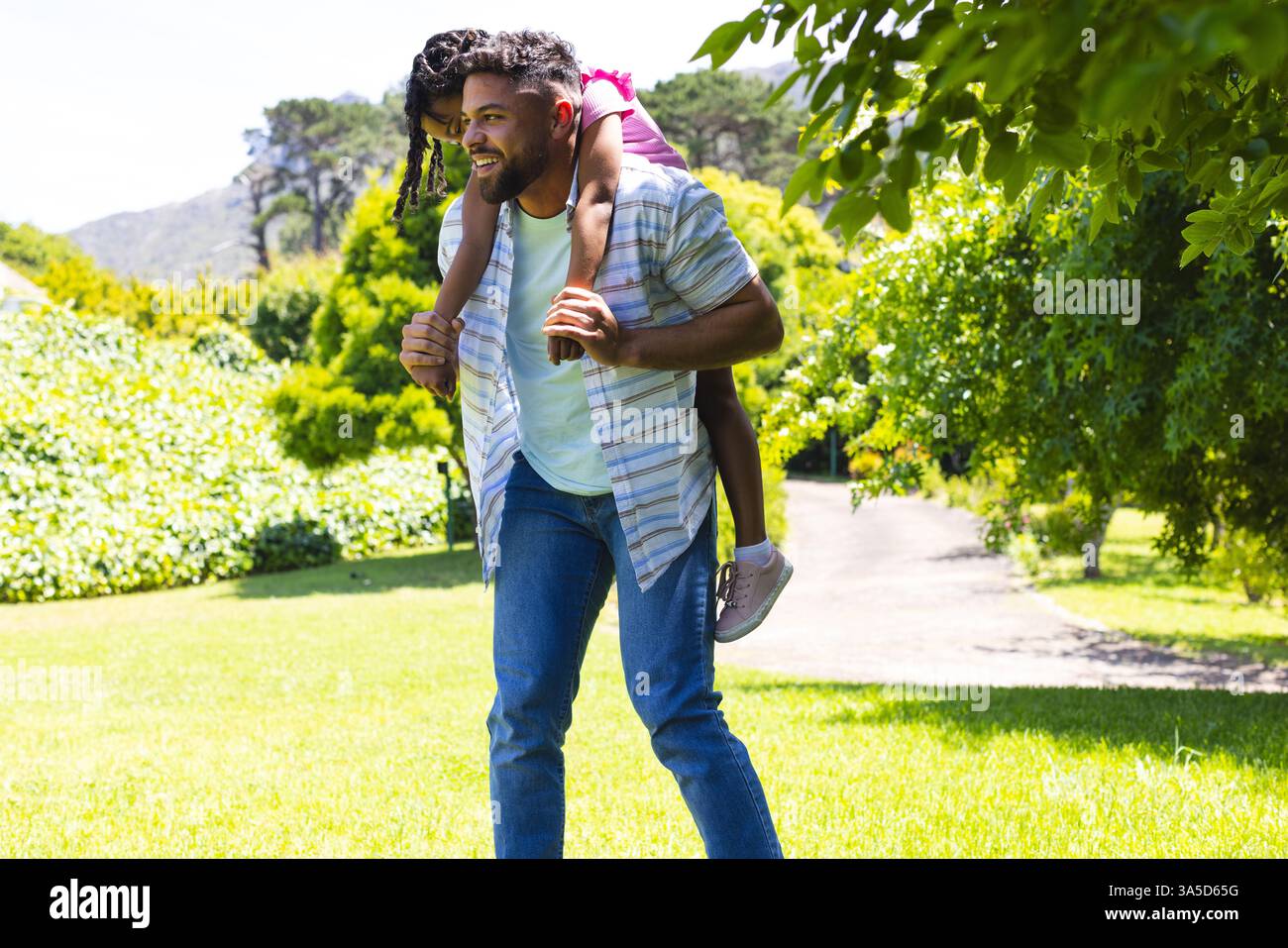 Father giving daughter piggyback ride in sunny park, both laughing ...