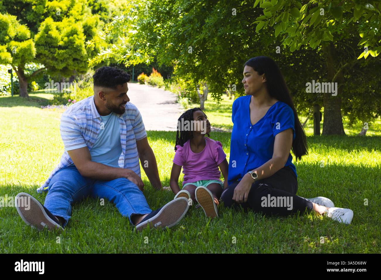 Family enjoying quality time sitting on grass in sunny park, smiling ...