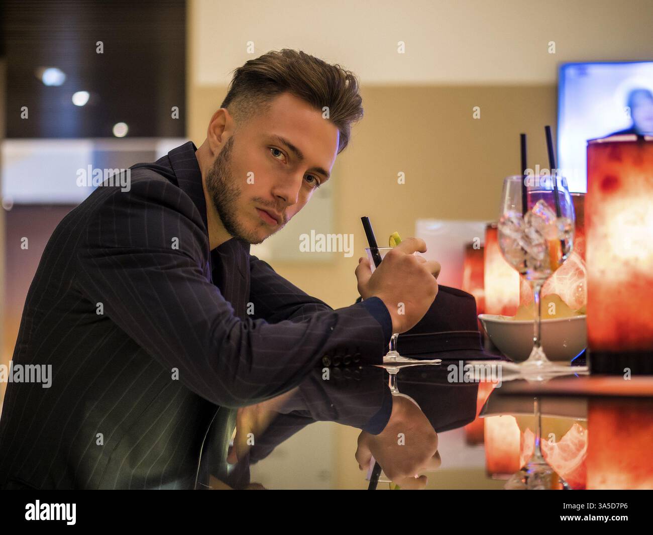 Handsome young man drinking cocktail at bar counter, wearing business ...