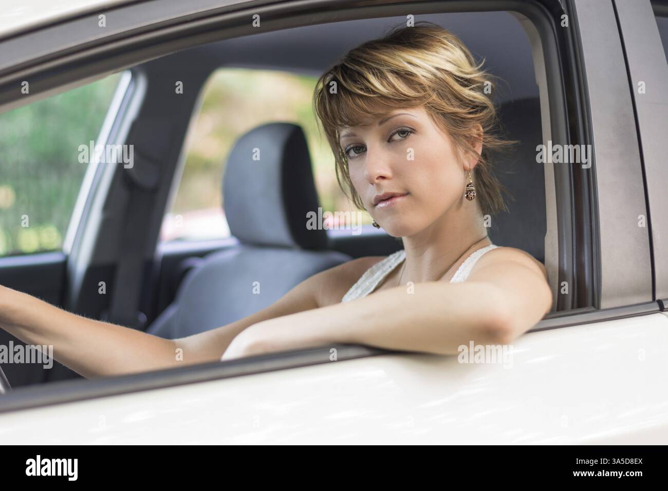 Serious pretty blonde young woman driving car looking at camera hi-res ...