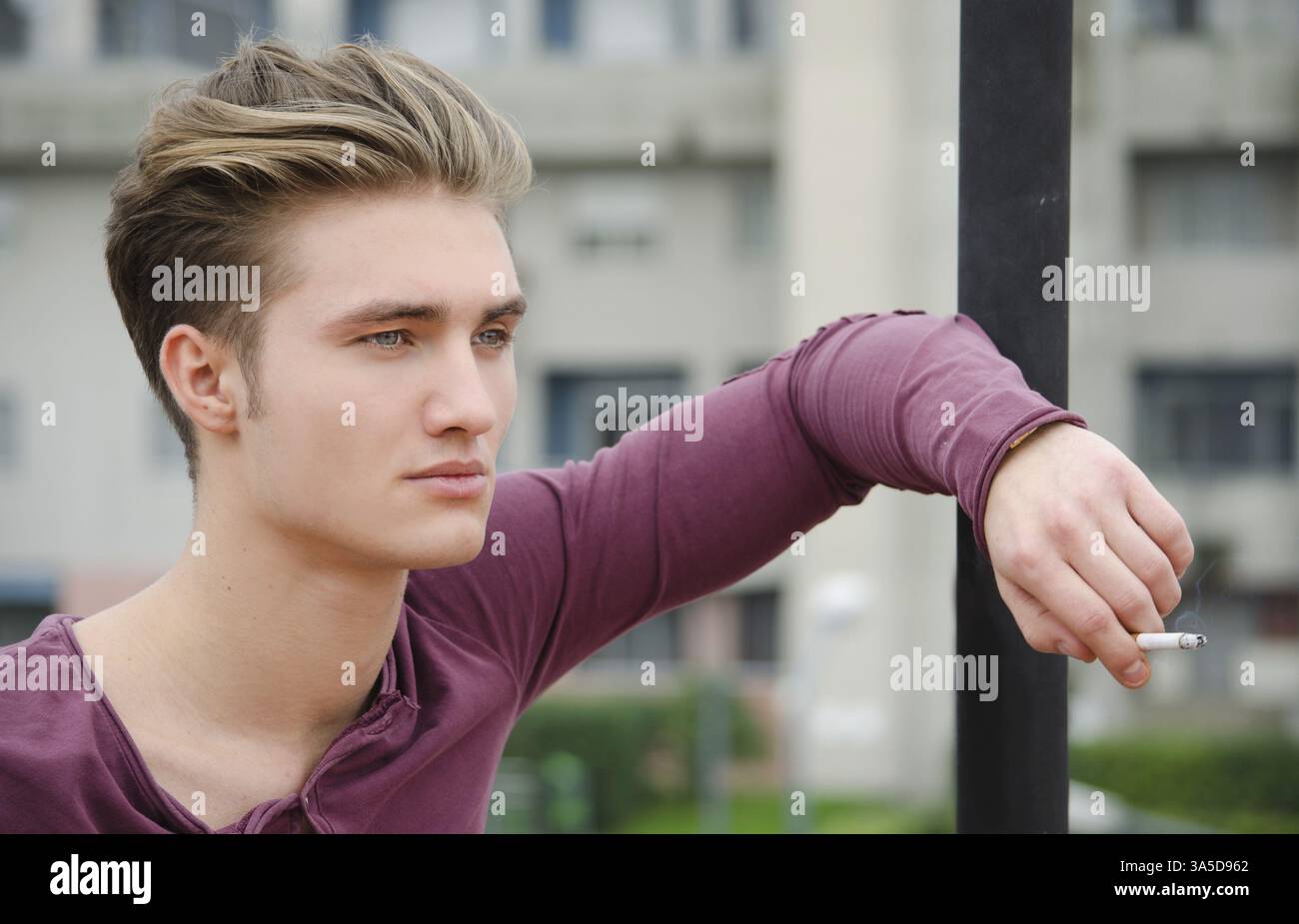 Attractive blue eyed, blond young man smoking cigarette outdoors ...