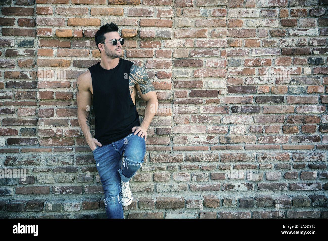 Attractive muscular man standing outdoor leaning against old brick wall ...