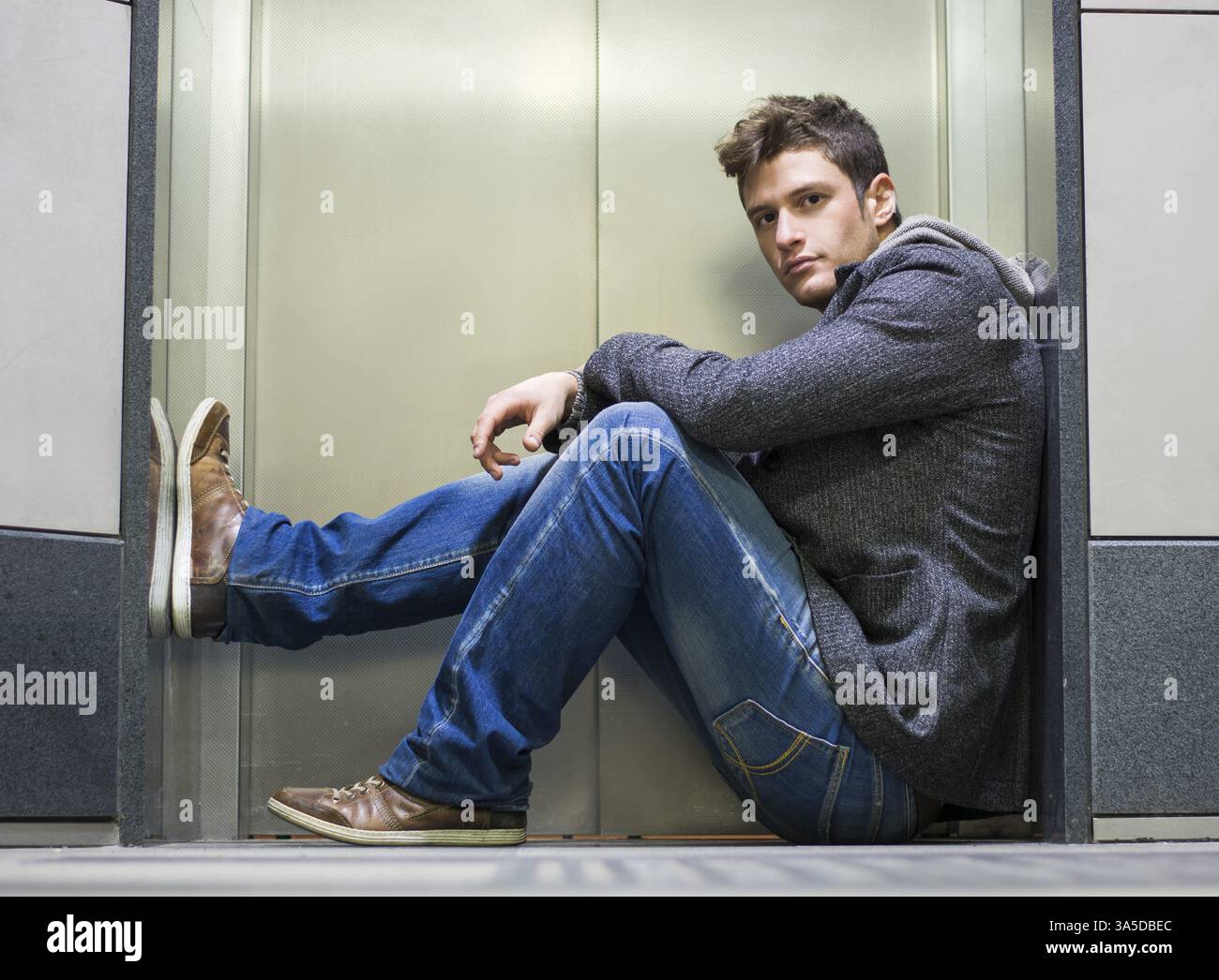 Handsome young man sitting in front of elevator lift doors hi-res stock ...