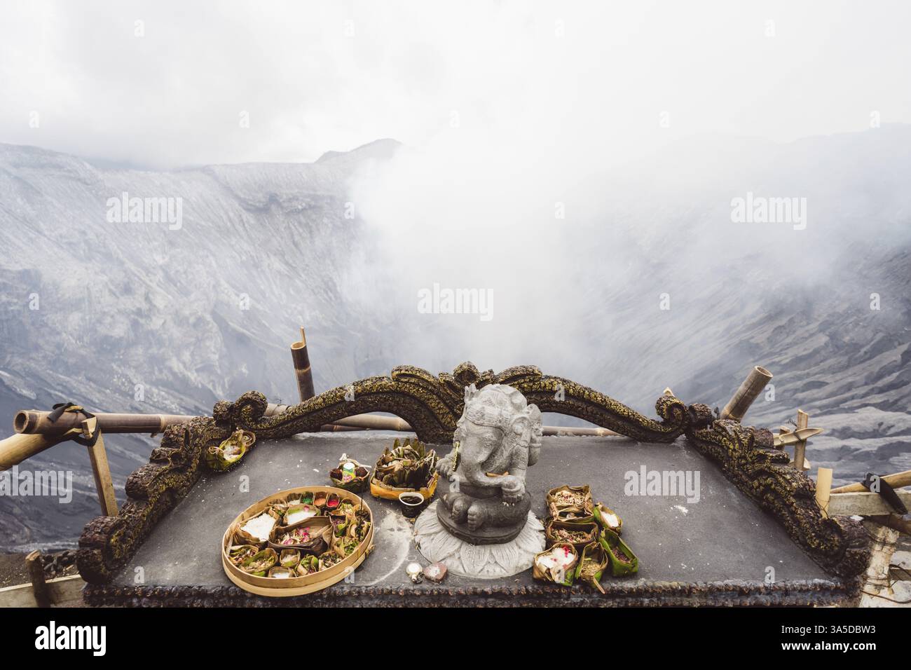 Traditional offerings and a statue on an altar with a misty volcano ...