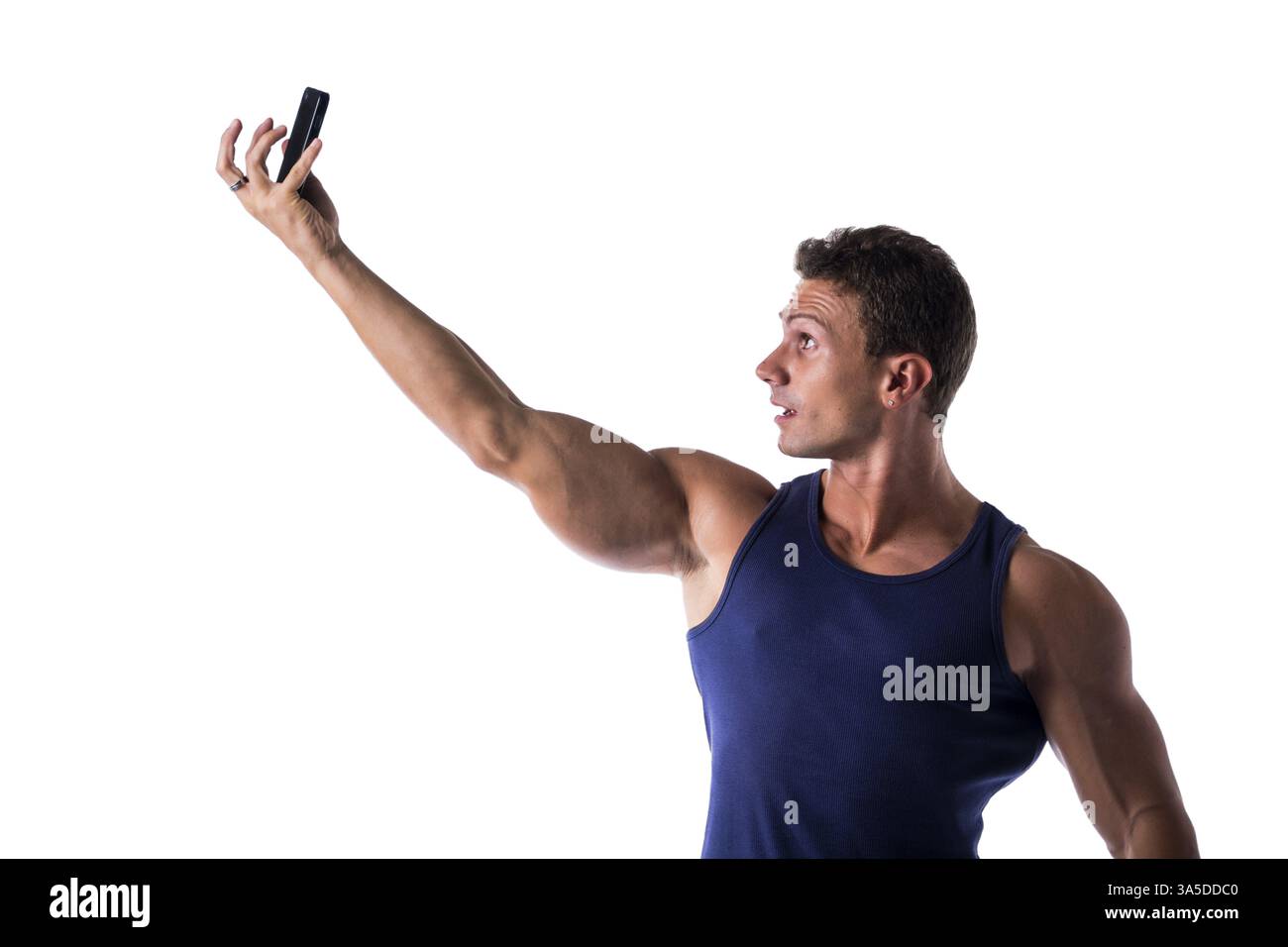 Handsome muscular young man taking selfie with cell phone while striking bodybuilding pose ...
