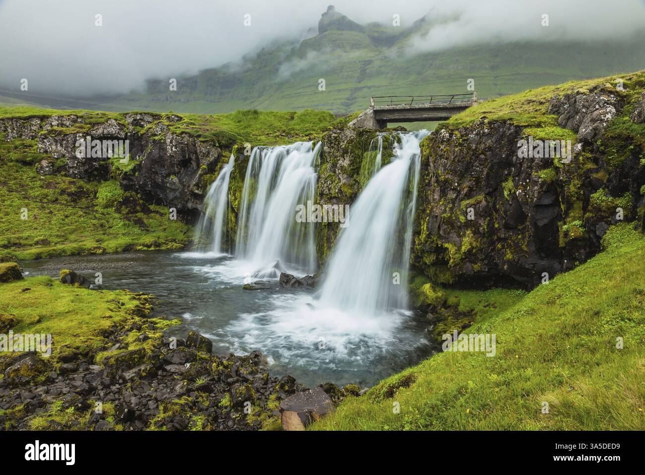 Threaded full-flowing waterfall on the grassy mountains. Iceland ...