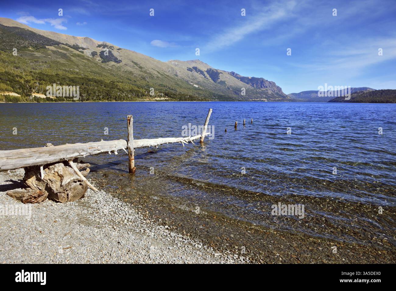 Wooden boat dock on the lake with the cold blue water and pebble beach ...