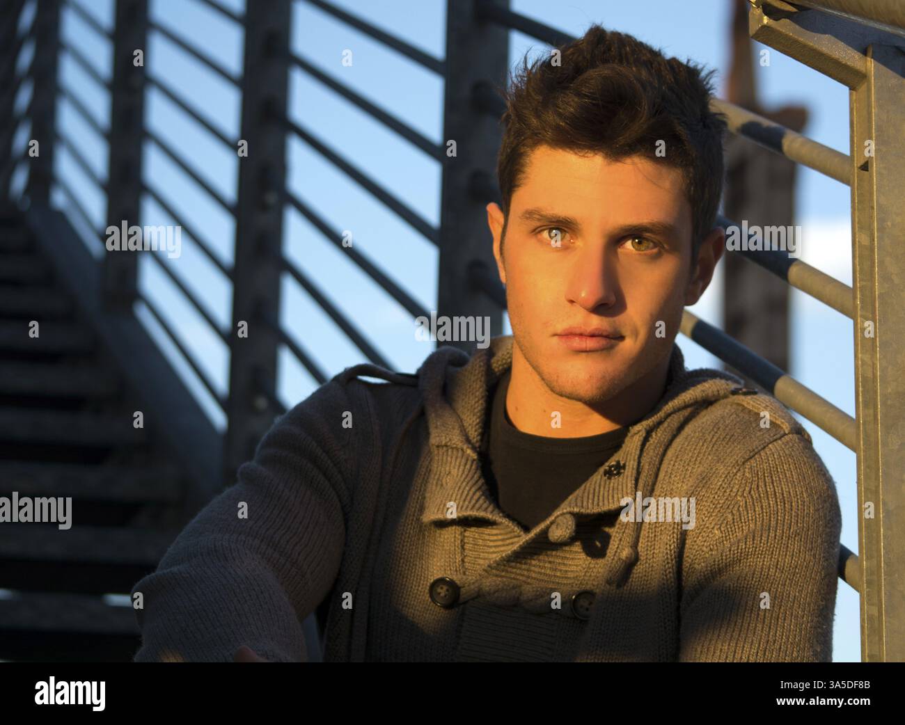 Headshot of handsome young man, lit by sunset light, leaning against ...