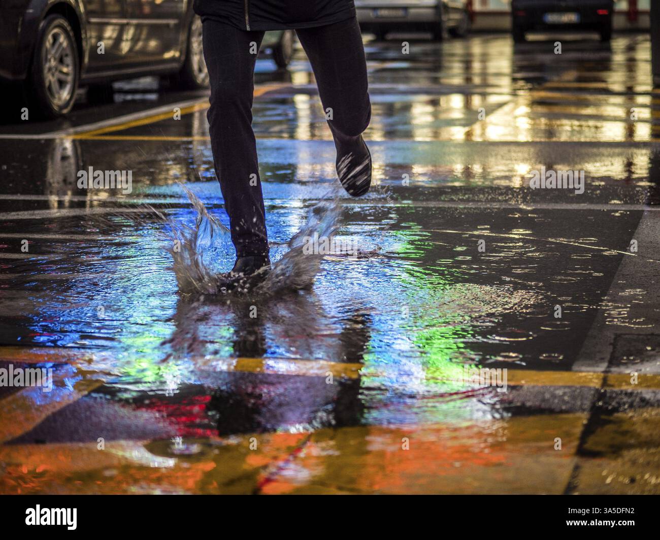 Crop shot of man splashing water in puddle on pavement reflecting night ...