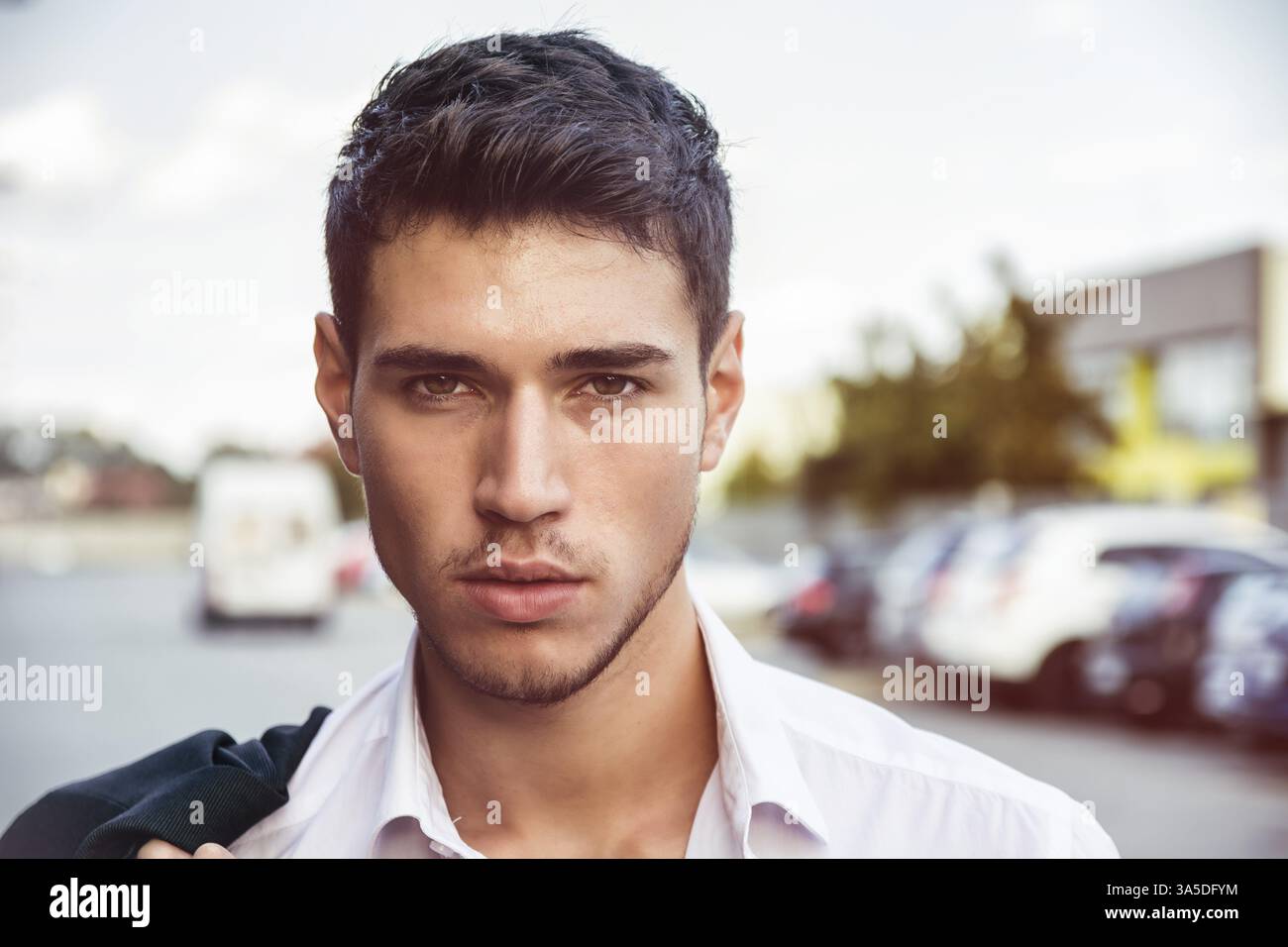 Headshot of handsome young man with white shirt in city street, lit by ...