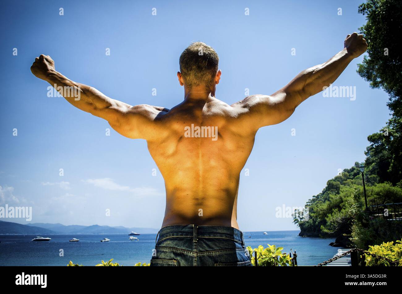 Back of young muscle man at the seaside, outdoors, showing muscular ...