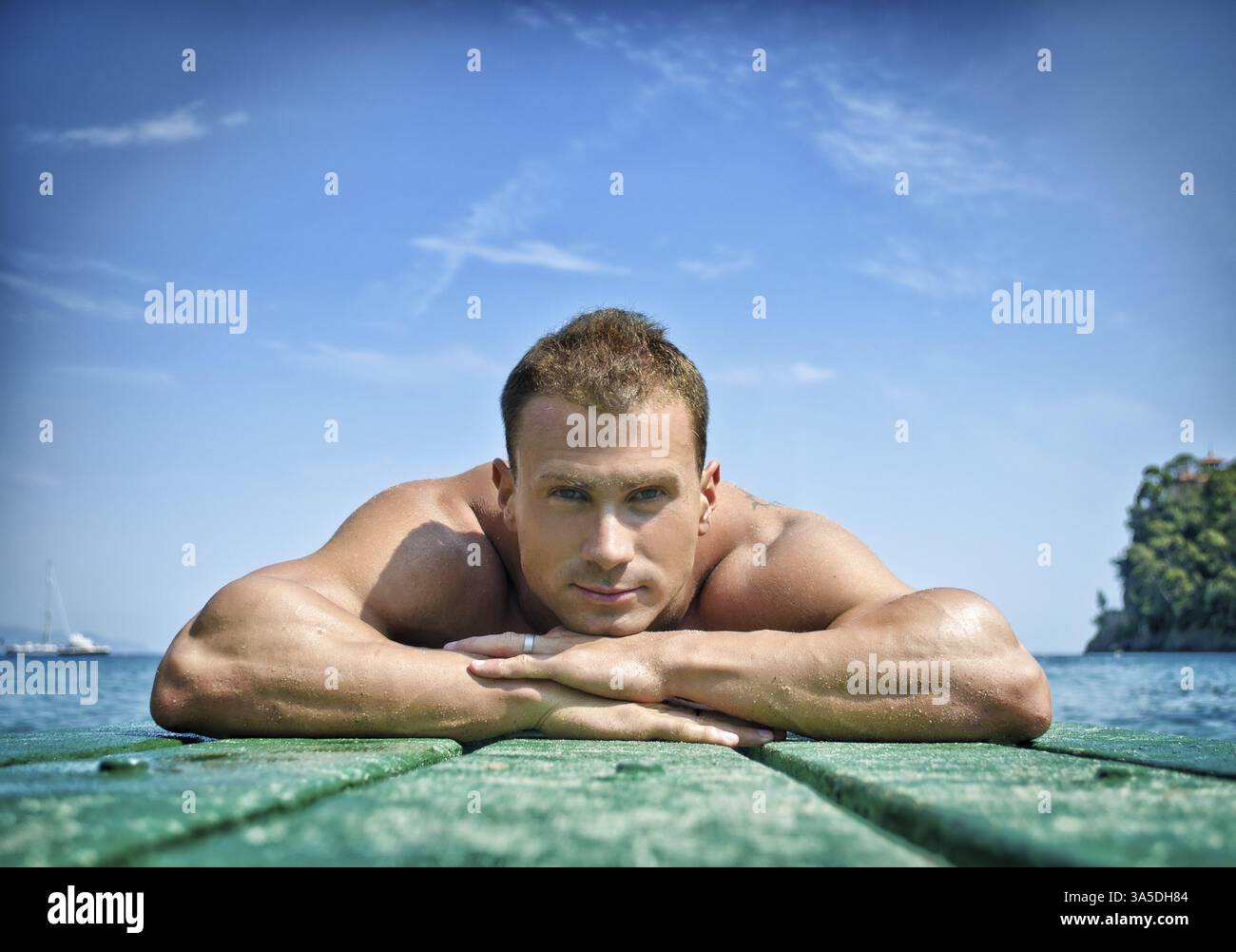 Muscular and handsome young man resting his chin on his hands, laying ...