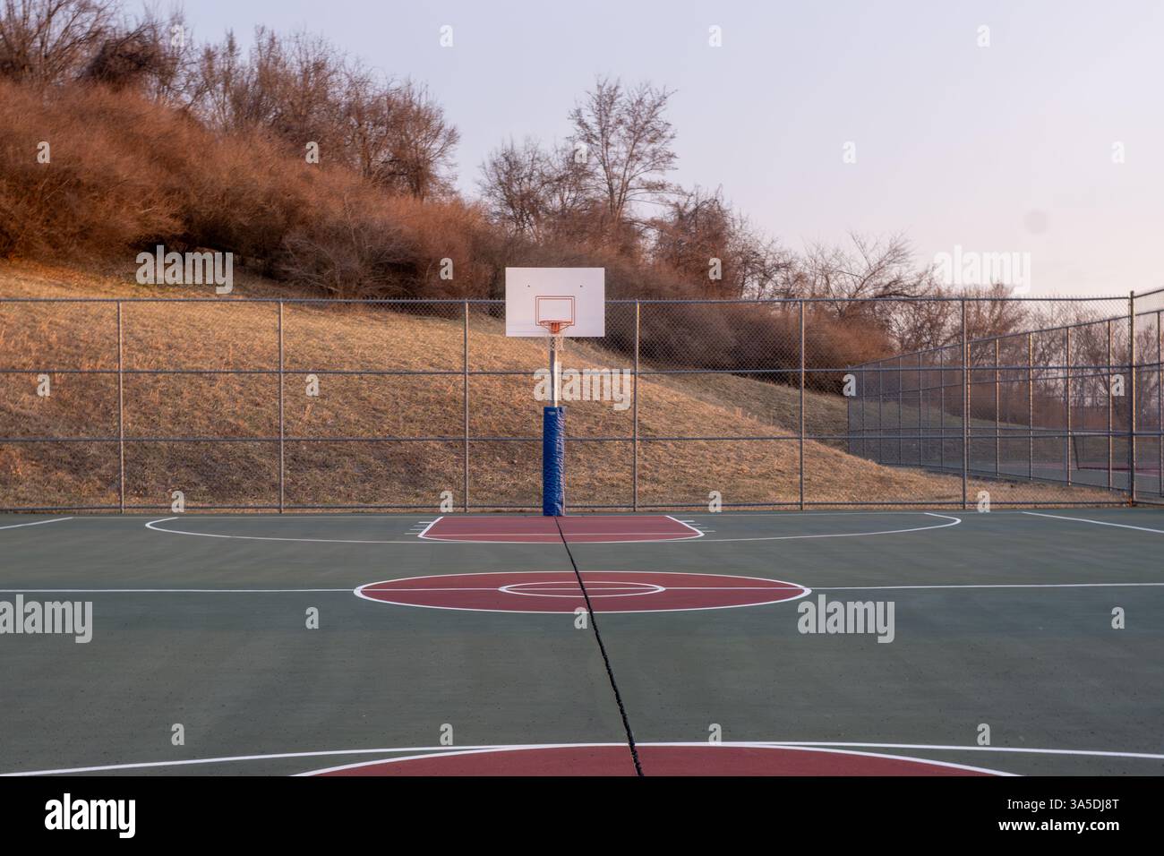 Quiet basketball court with a single hoop at dusk, surrounded by ...