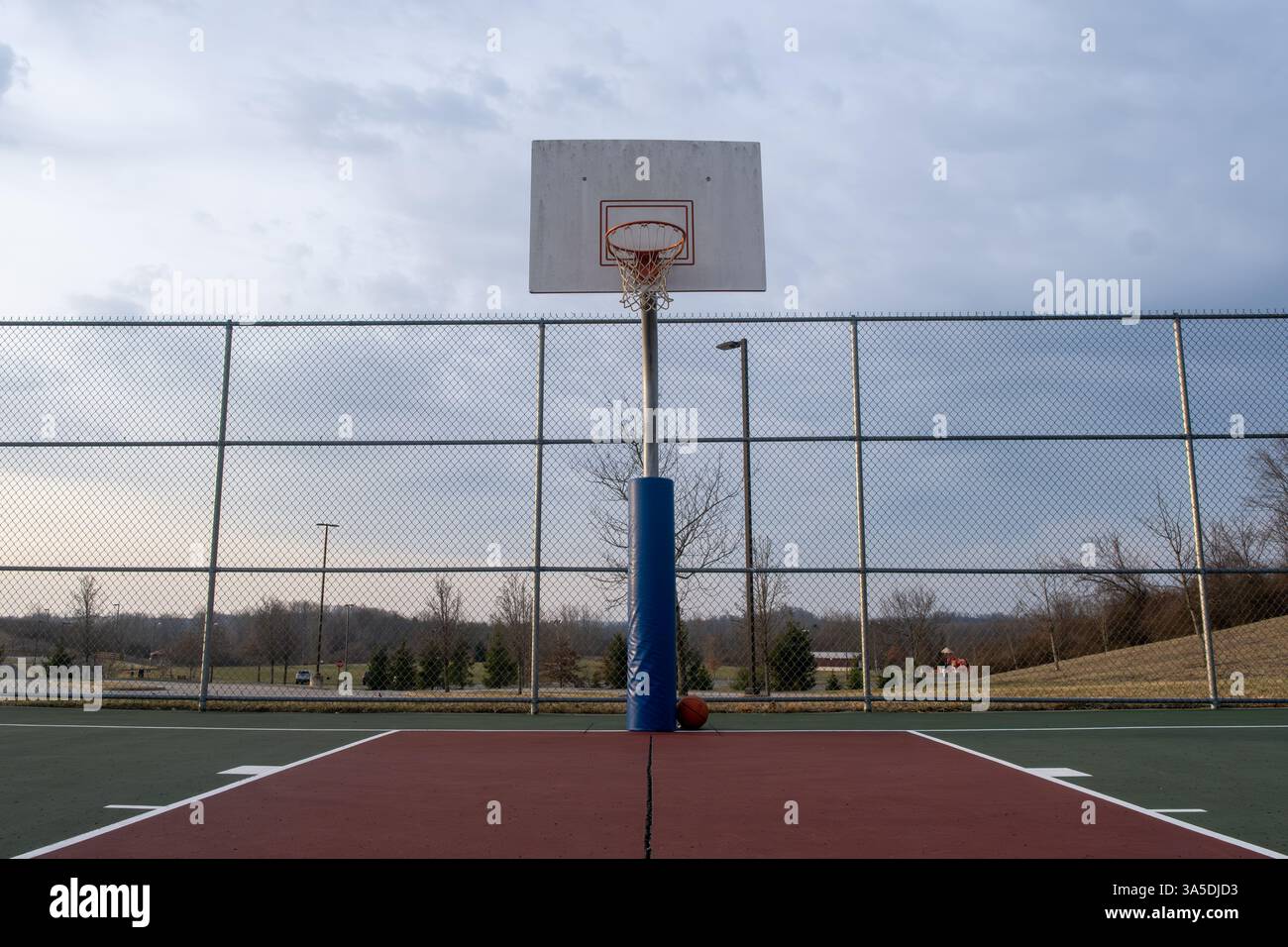 Empty basketball court features a hoop and ball against a grey sky ...