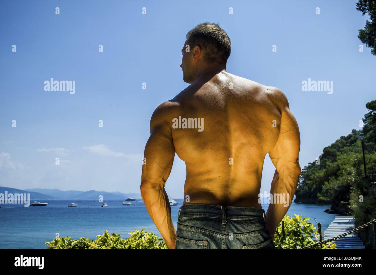 Back of young muscle man at the seaside, outdoors, showing muscular ...