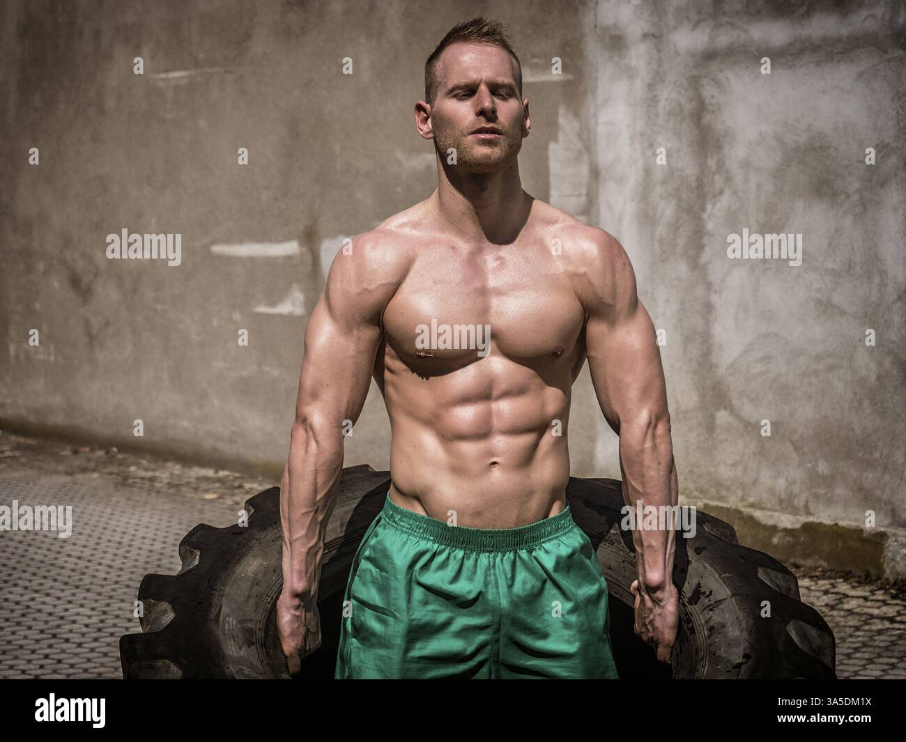 Handsome muscular young man exercising, flipping big truck tire outdoor ...