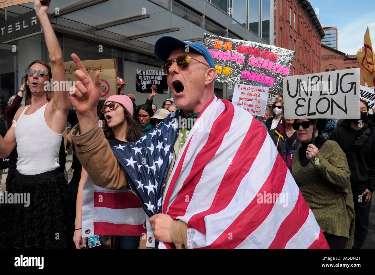 An anti-Elon Musk demonstrator draped in the American flag chants ...