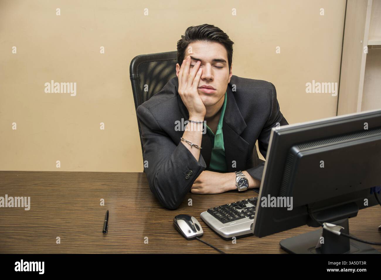 Tired bored young businessman sitting at his desk in front of his ...