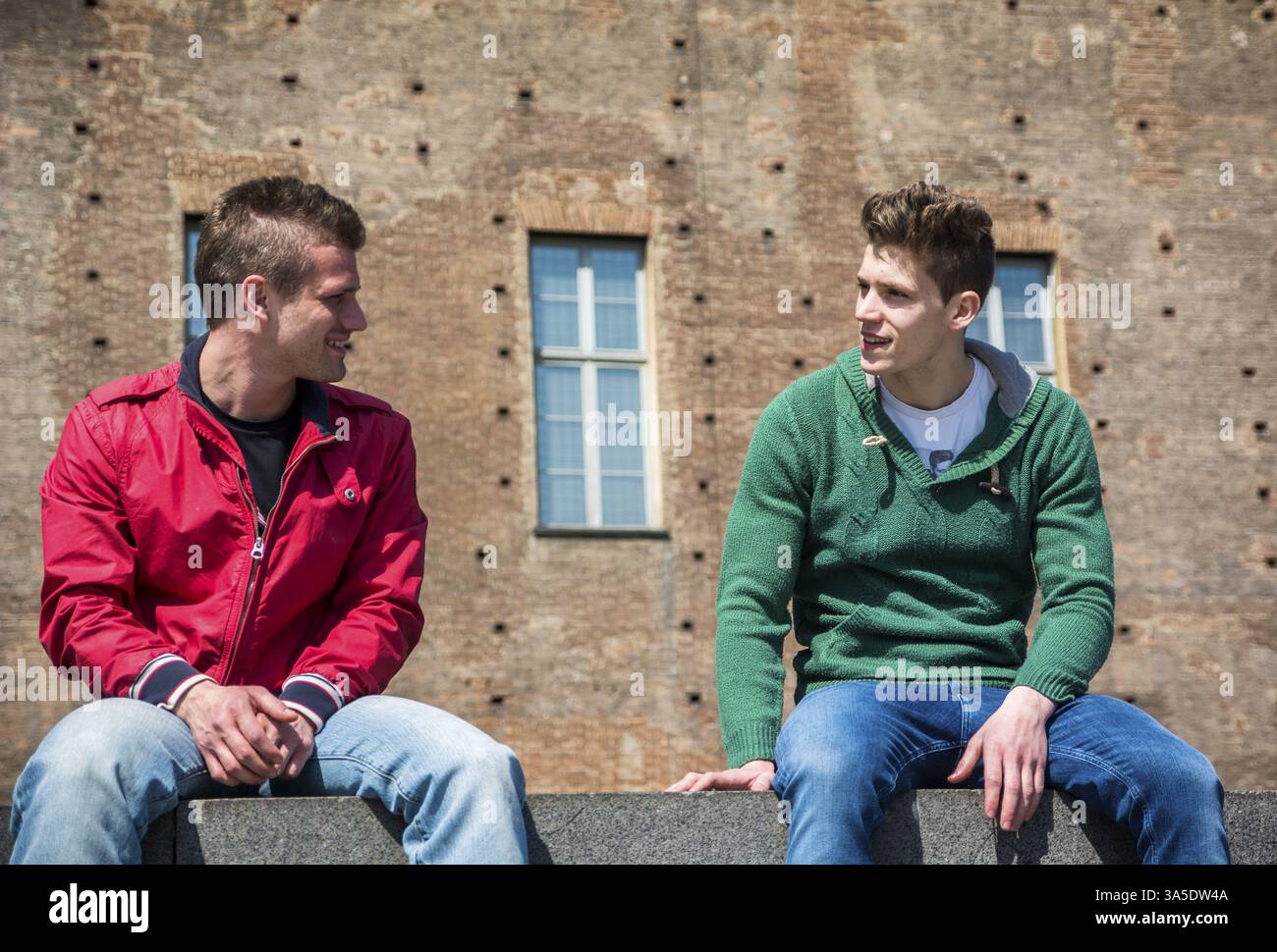 Two young men talking while sitting on curb. Summertime Stock Photo - Alamy