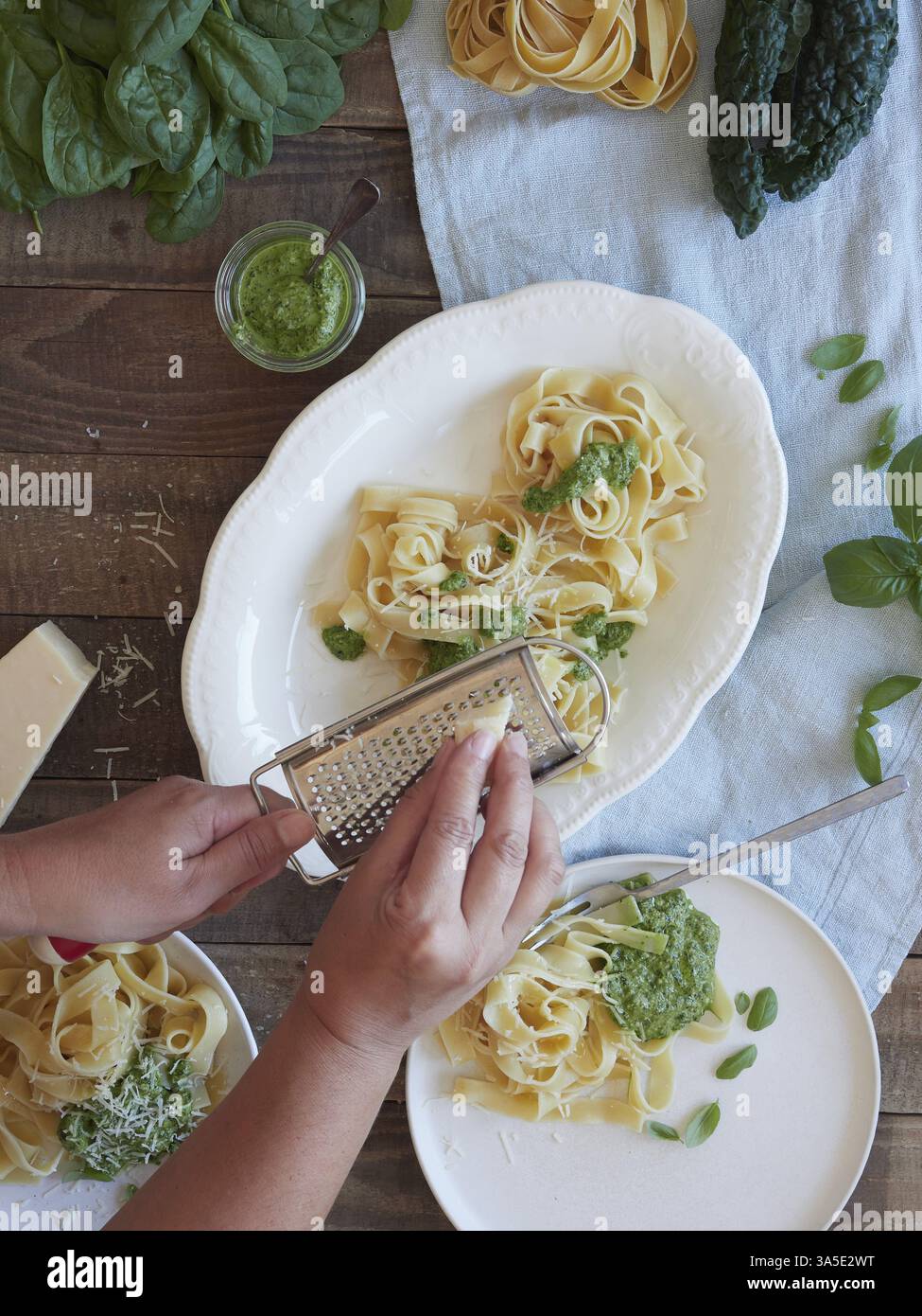 Hands grating Parmesan cheese over a platter of Tagliatelle pasta with ...