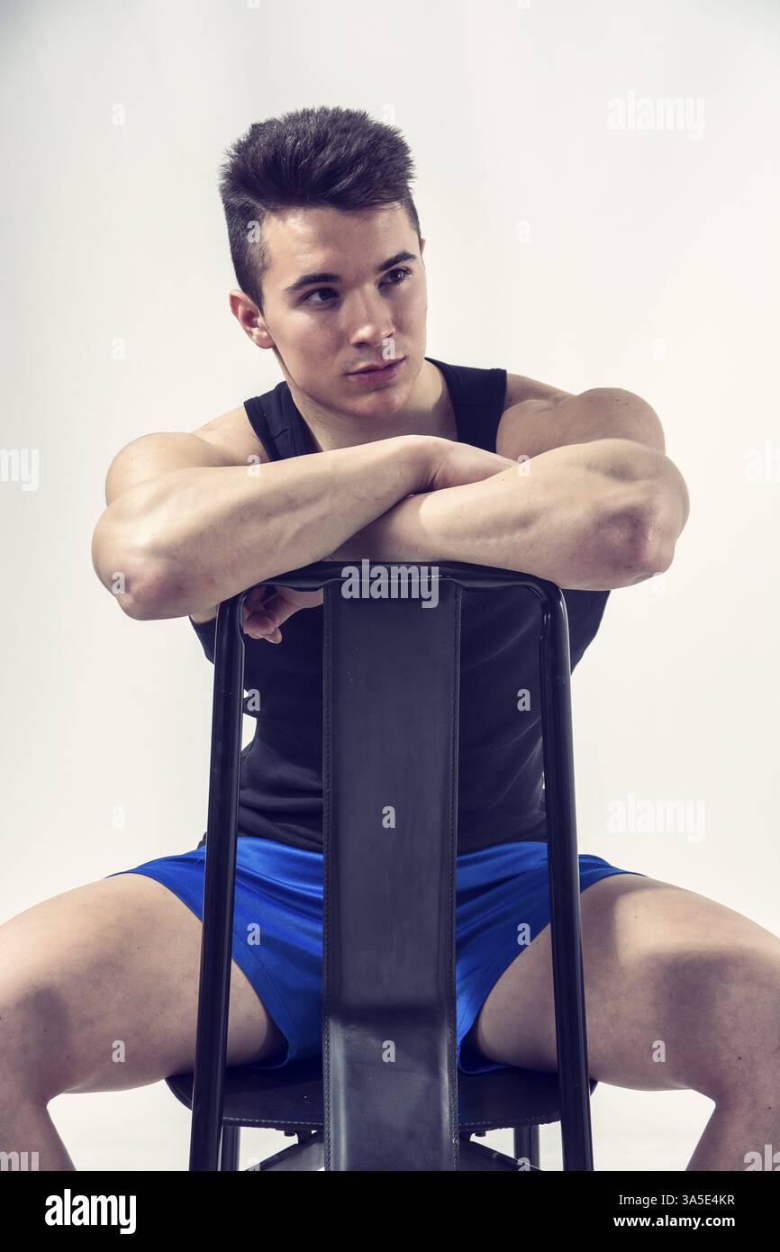 Handsome young muscular man sitting on chair in studio shot over neutral background Stock Photo ...