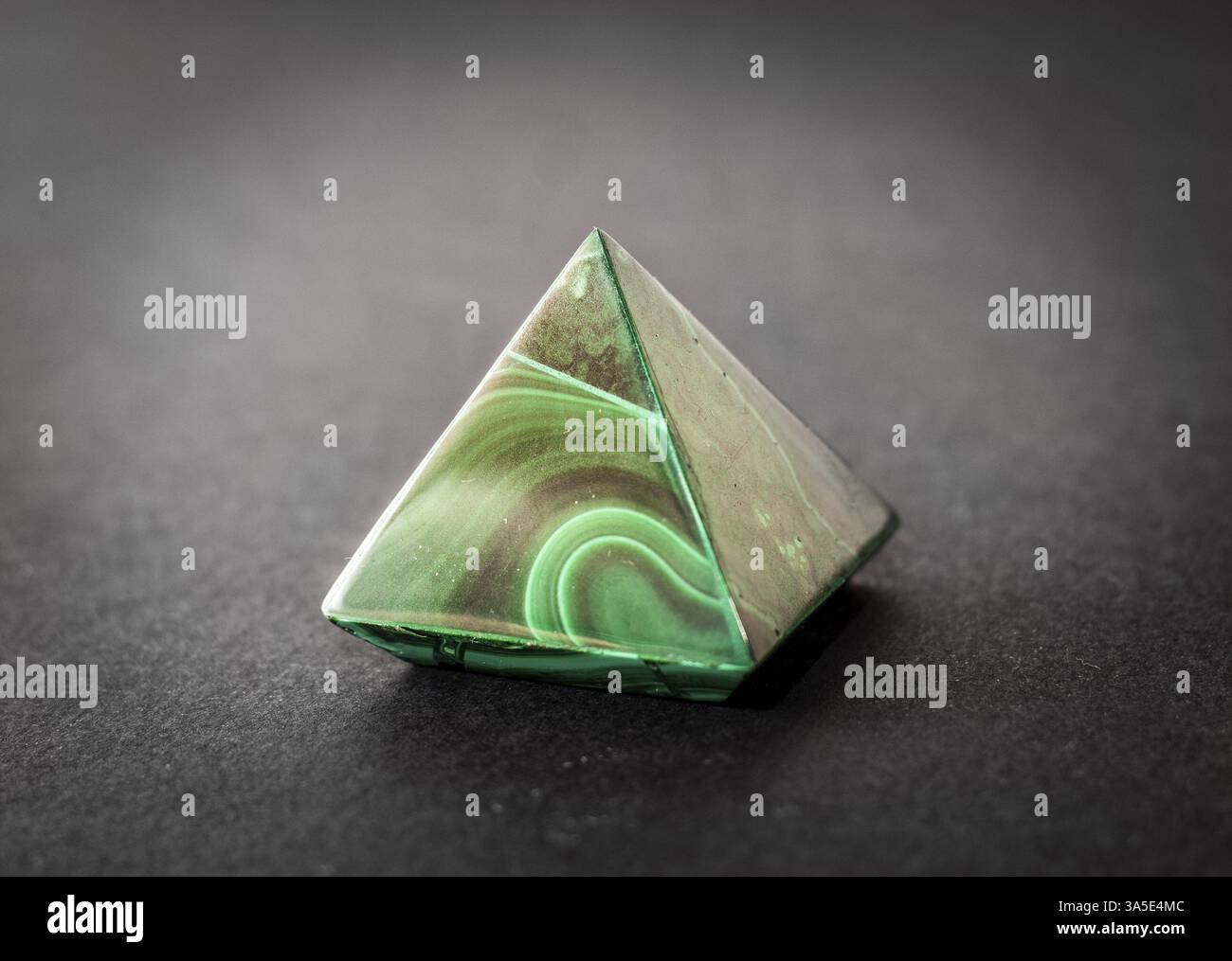 Beautiful malachite pyramid, cut mineral on dark background or surface ...