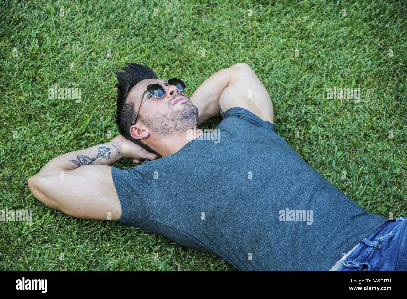 Good looking, fit male model relaxing lying on the grass, looking at ...