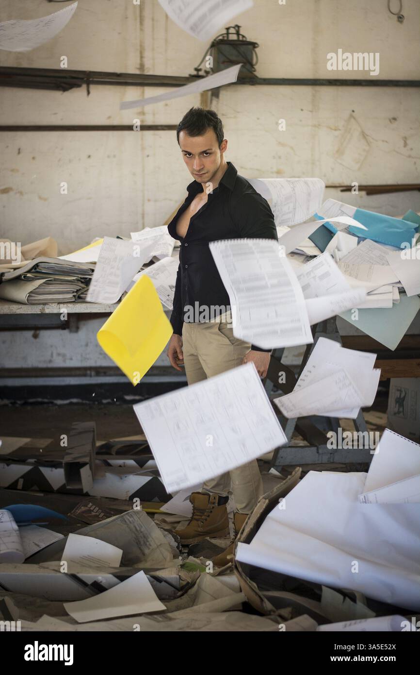 Attractive serious young man in very messy office with documents flying ...