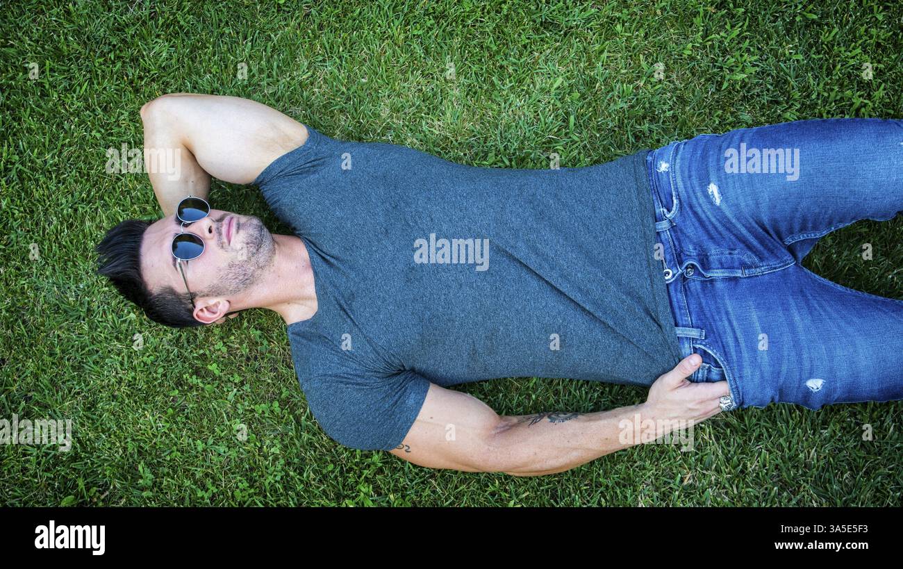 Good looking, fit male model relaxing lying on the grass, looking at ...