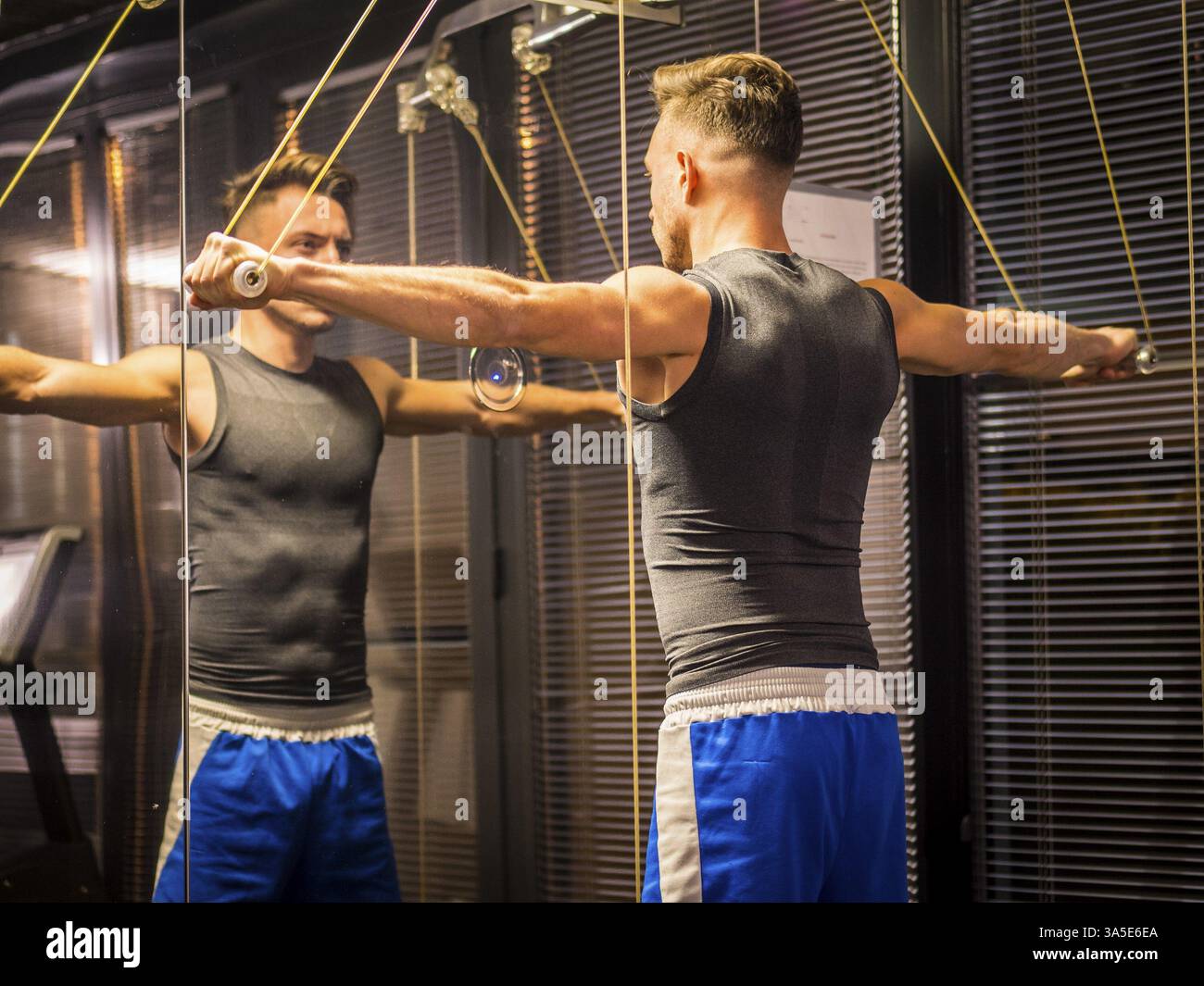 Muscular young man, training shoulders on gym cable machine Stock Photo ...