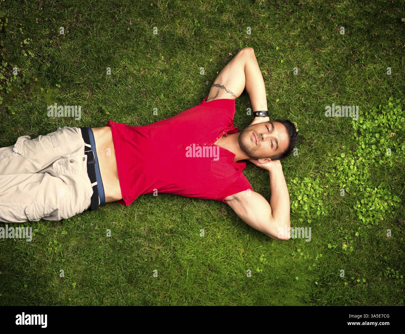 Good looking, fit male model relaxing lying on the grass, looking at ...