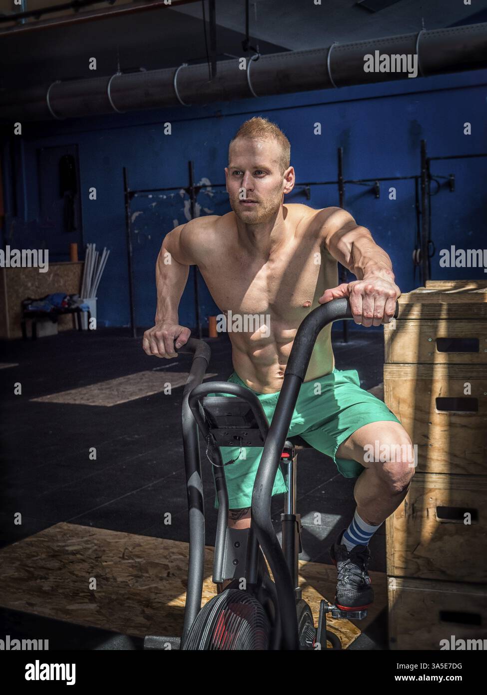 Hunky muscular blond male bodybuilder exercising on stationary bike in ...