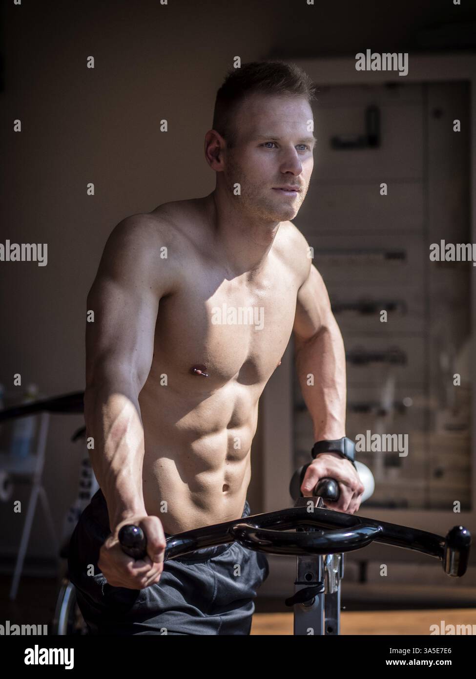 Hunky muscular blond male bodybuilder exercising on stationary bike in ...