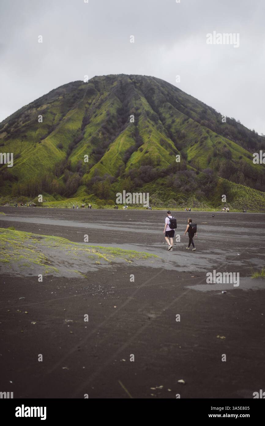 Two people walking in front of a volcano covered with green vegetation ...