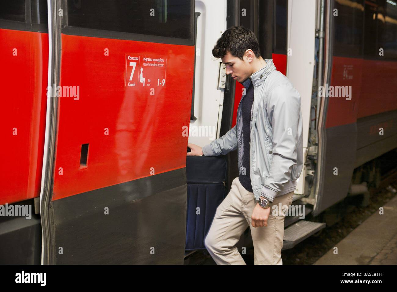 Handsome young man getting aboard on train, standing in open door ...